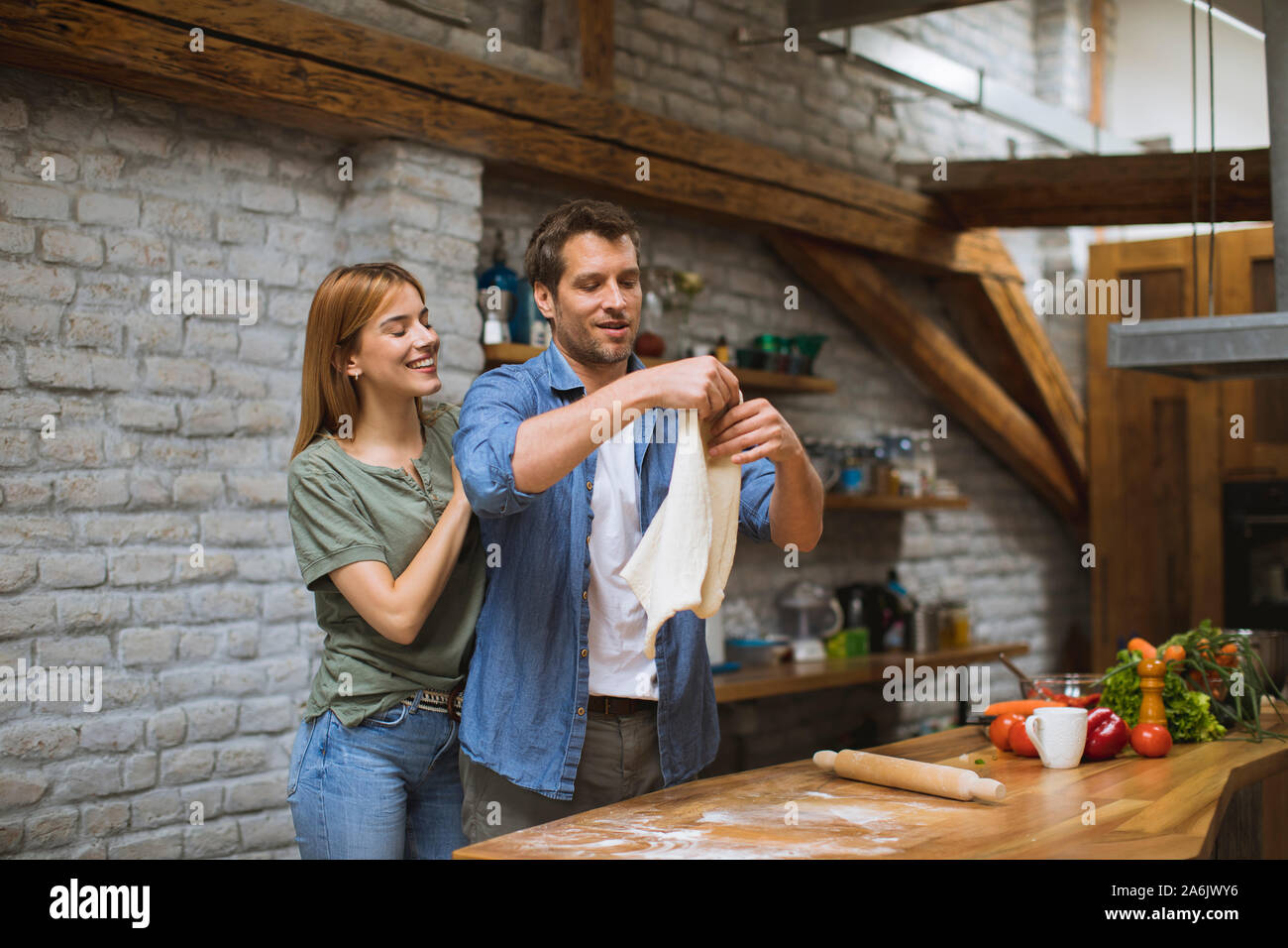Cheerful young couple making pizza in rustic kitchen together Stock ...