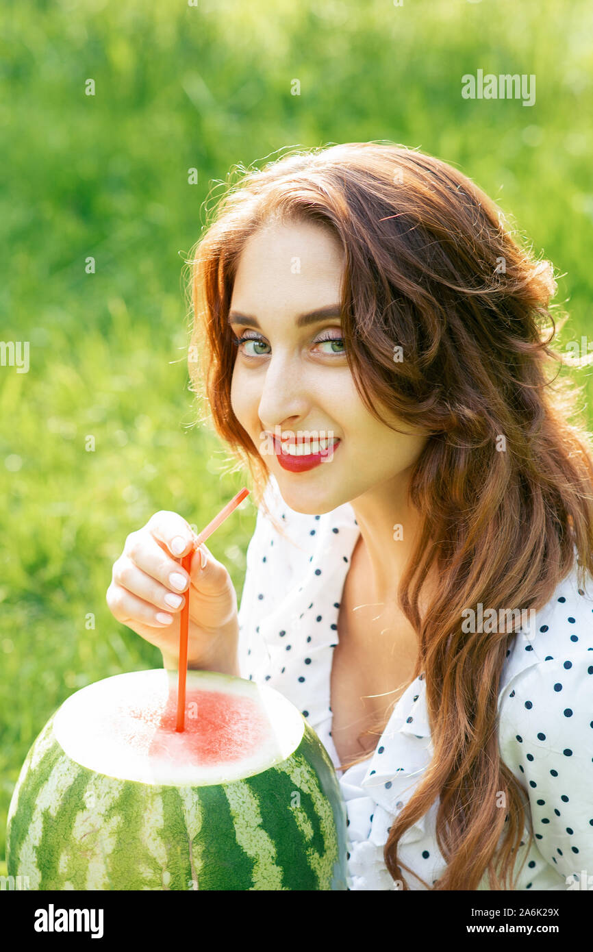 Woman in white dress holds watermelon with cocktail straw on grass ...