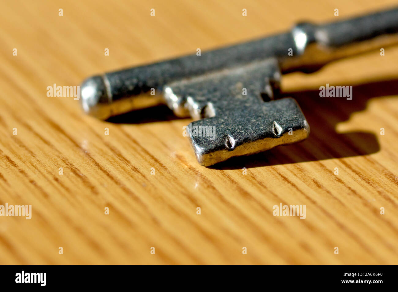 Close up of the bottom end of an old, steel key laying on a brown wood ...