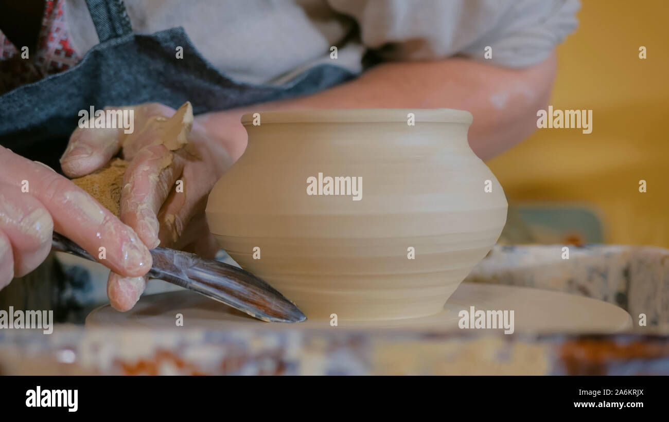 Professional potter carving pot with special tool in pottery workshop ...