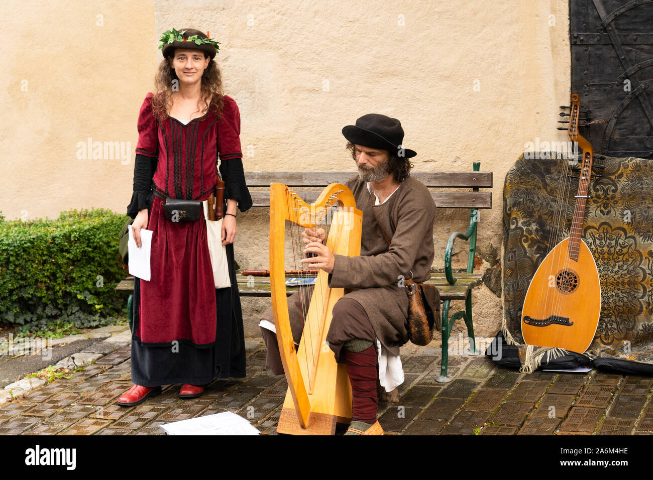 A man and woman in medieval clothes playing a harp and singing at the ...