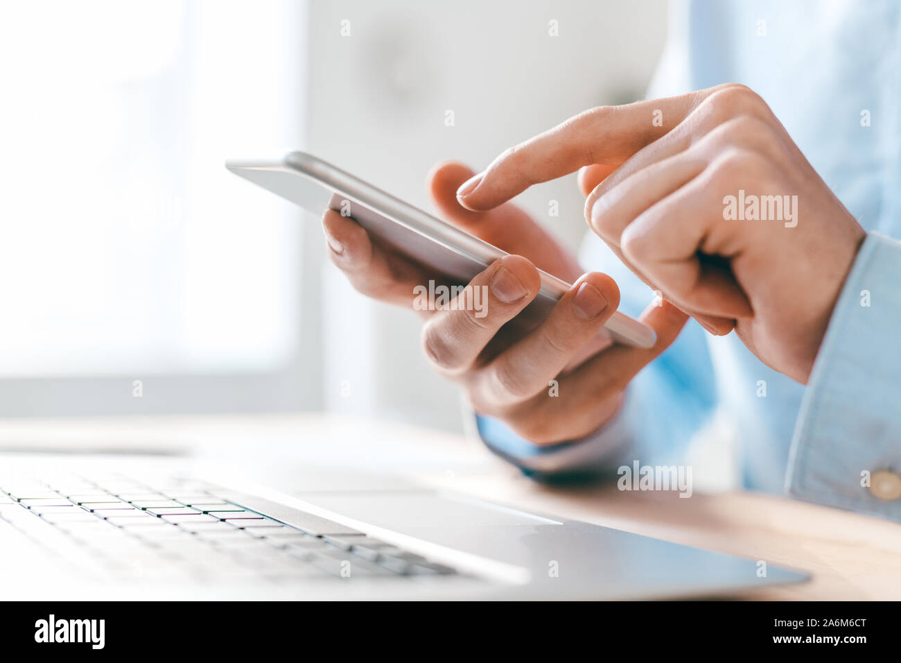 Hands of young businessman pointing at smartphone screen over laptop ...