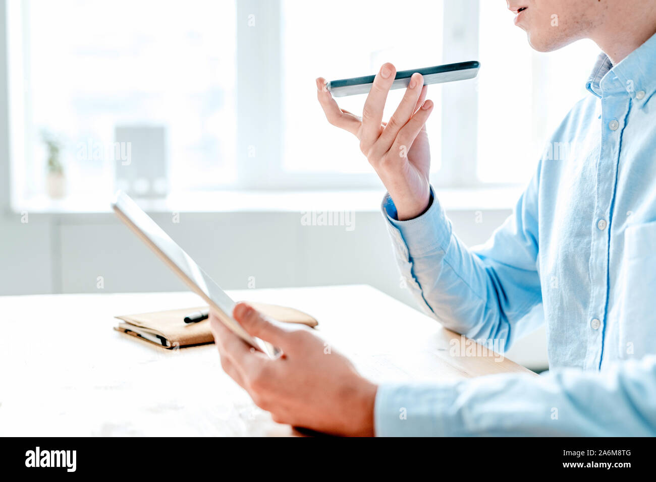 Young designer using touchpad and holding smartphone by his mouth Stock ...