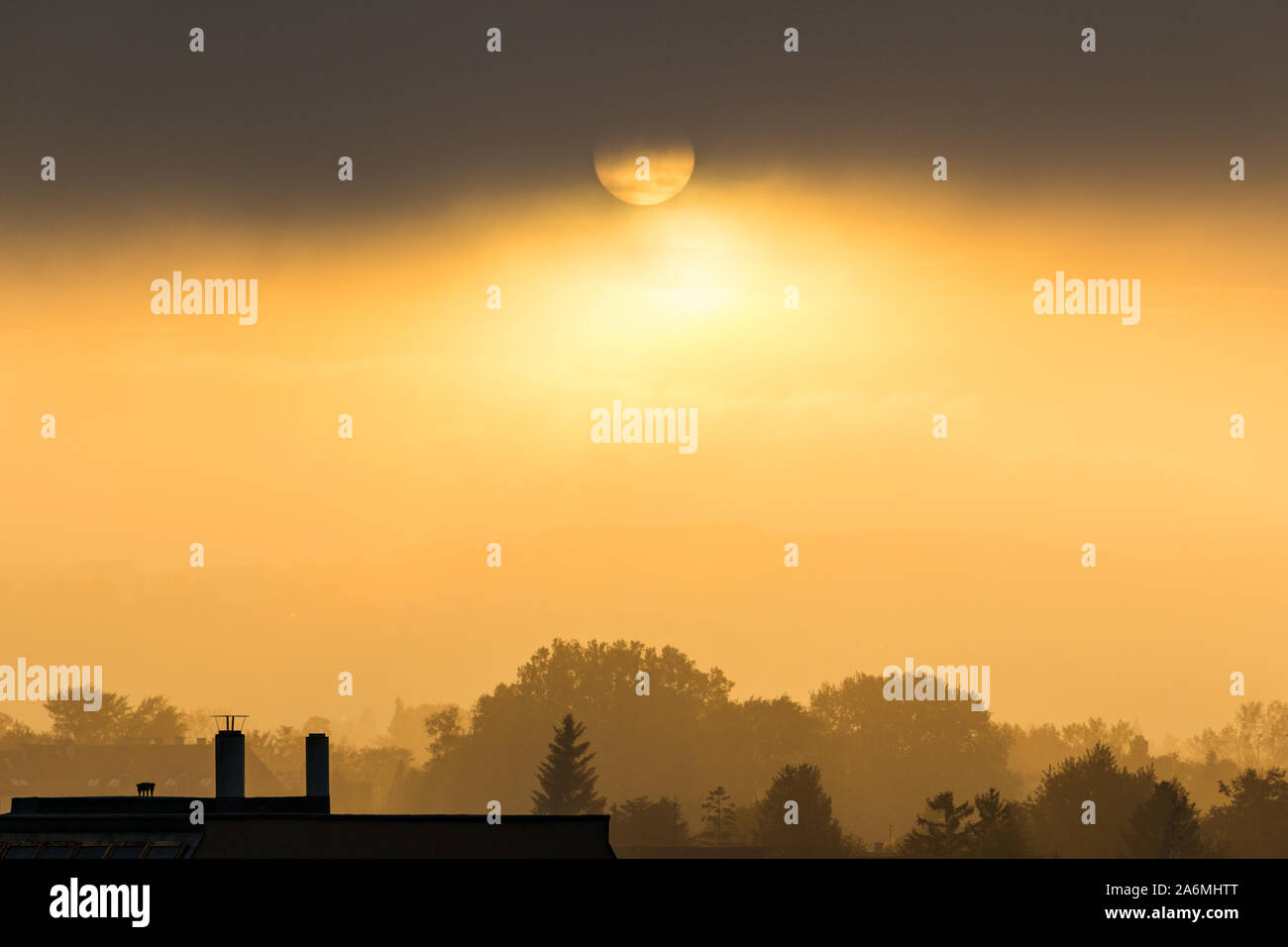 Sunset sun through fog mist with silhouette of roof and trees in autumn ...