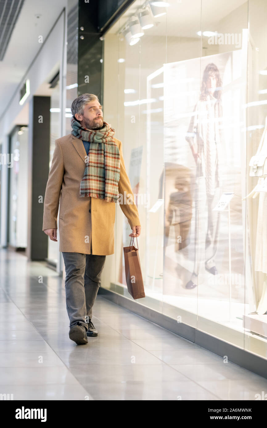 Middle aged man in stylish casualwear looking at one of large shop ...