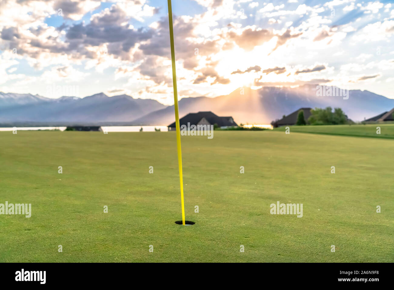 Yellow flagstick and hole at a golf course against lake mountain and ...