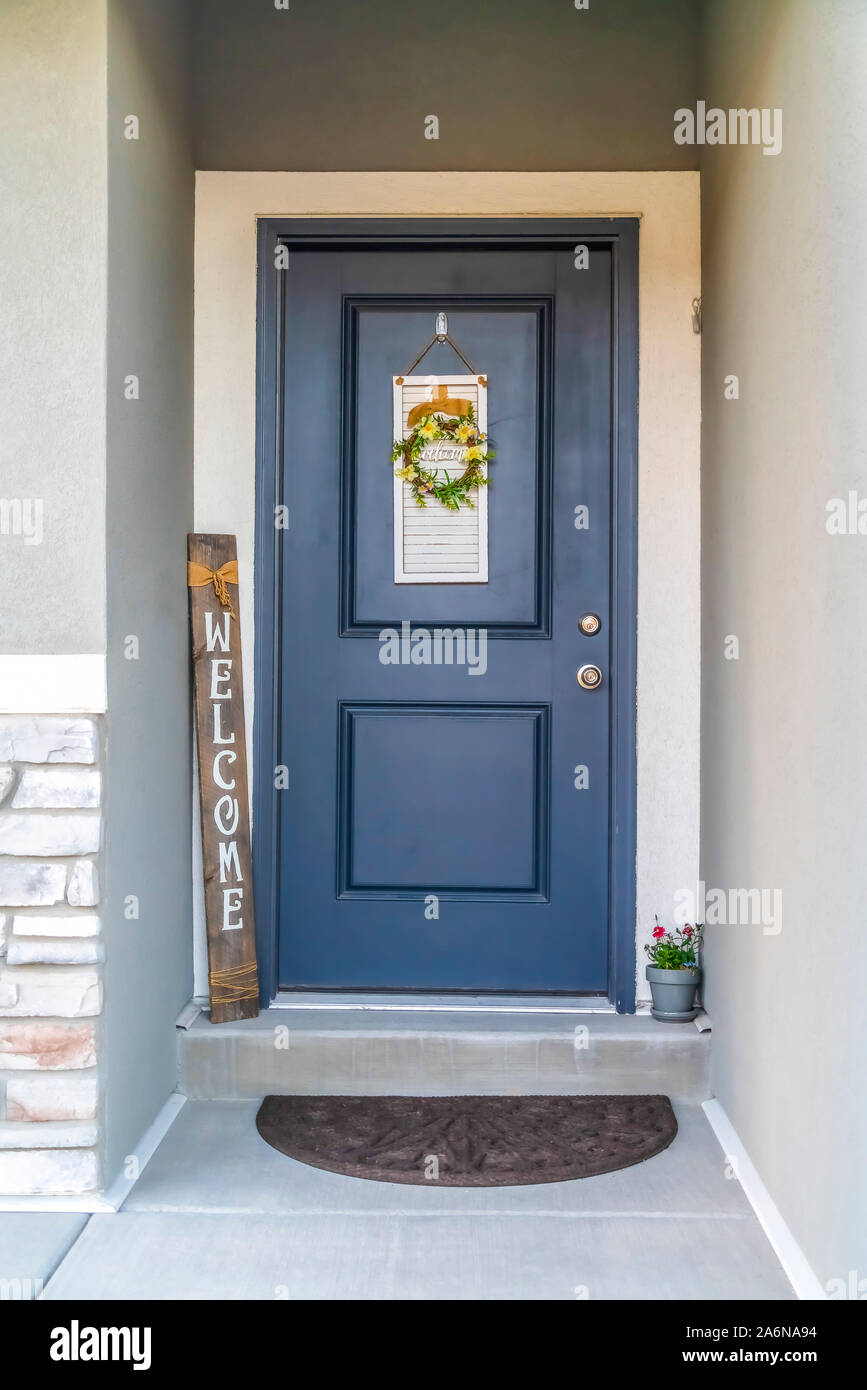 Blue front door of a home decorated with wreath welcome sign and potted ...