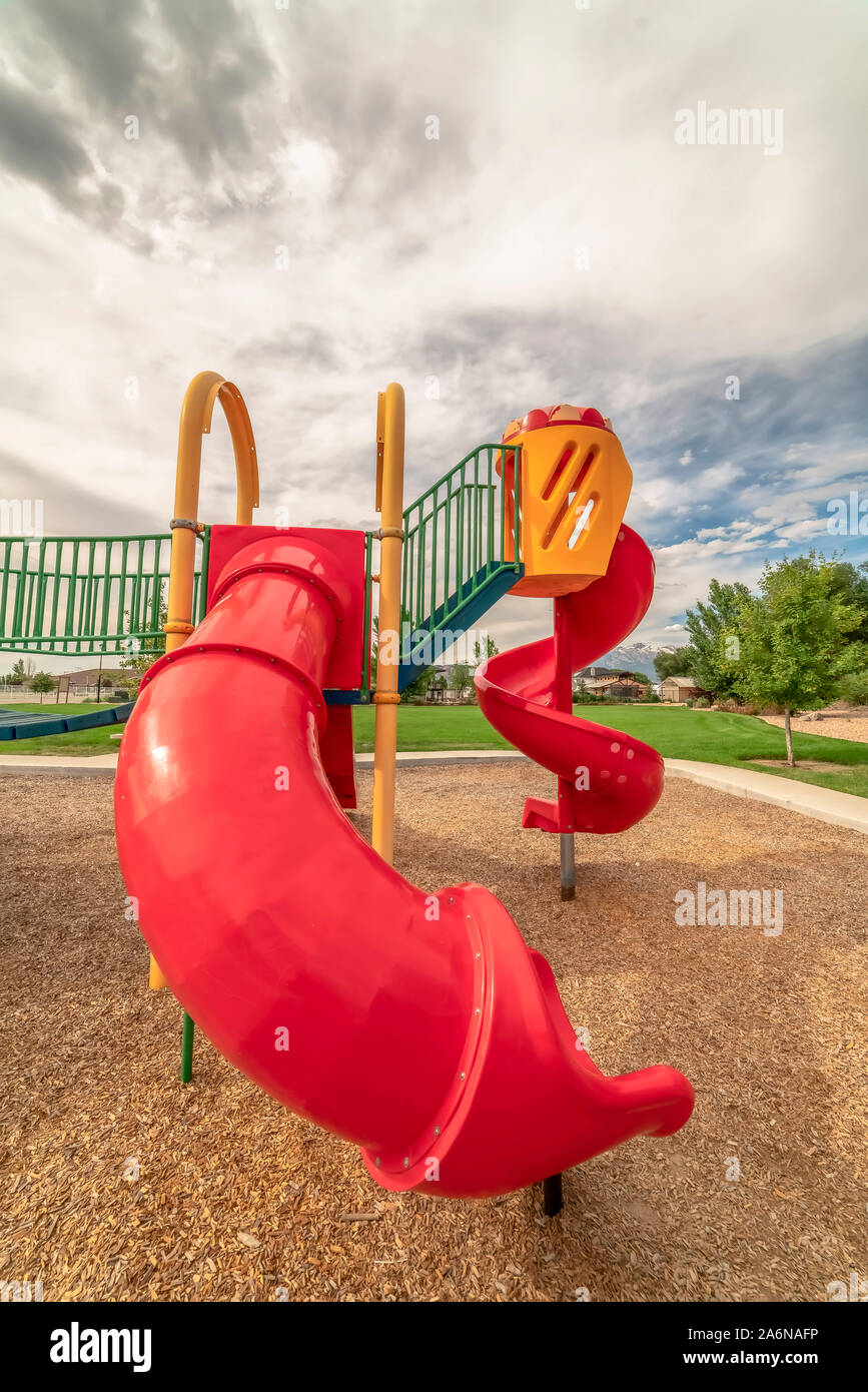 Red closed tube slide and spiral slide at a playground against cloudy ...
