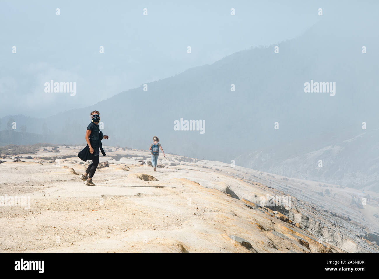Young women in protective mask walking by wastelands around Kawah Ijen ...