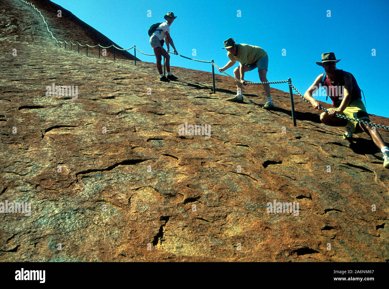 Three men climbing Uluru rock in central Australia 1990. The iconic ...