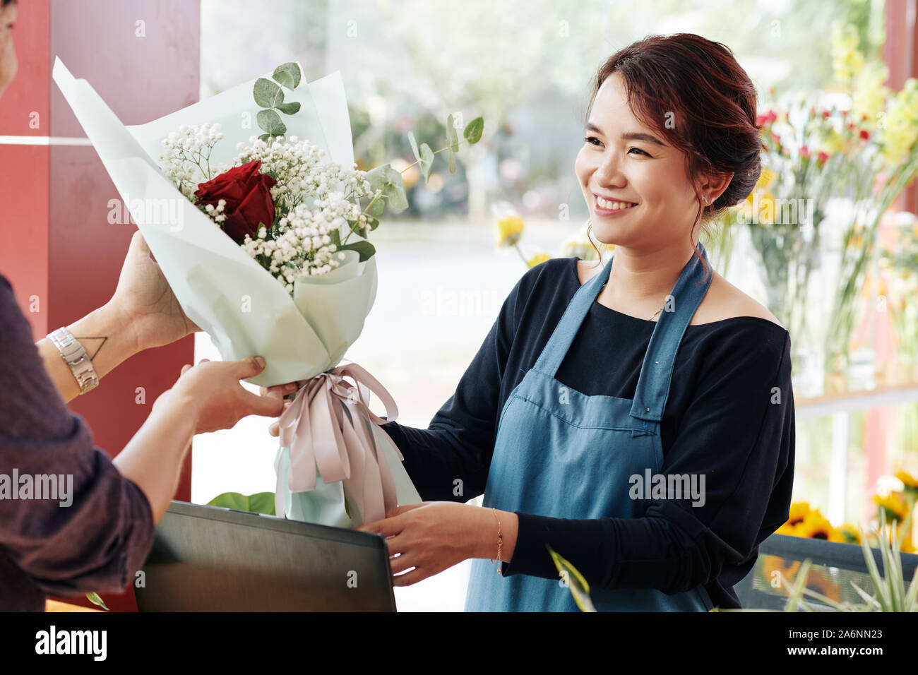 Positive flower shop worker giving beautiful bouquet with red rose to ...