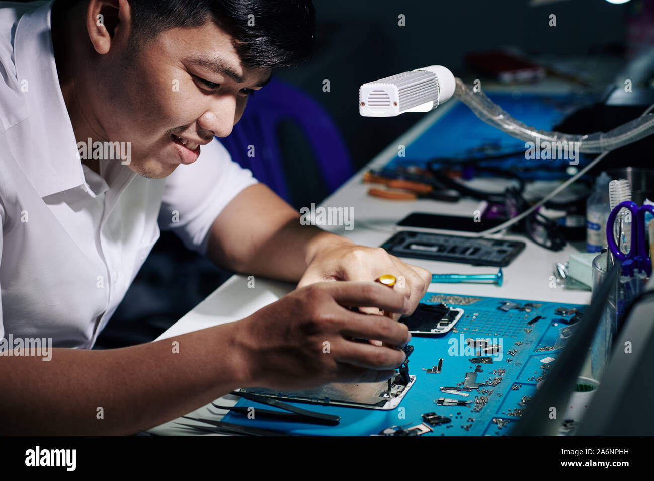 Smiling Asian man repairing smartphone under light of led lamp at his ...