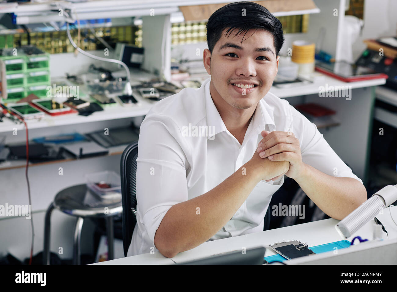 Portrait of young positive Asian repairman working at table at ...