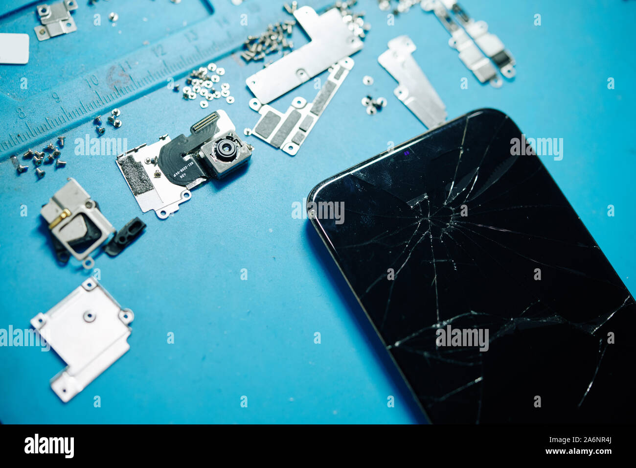 Cracked modern smartphone, broken camera, metal brackets and screws ...