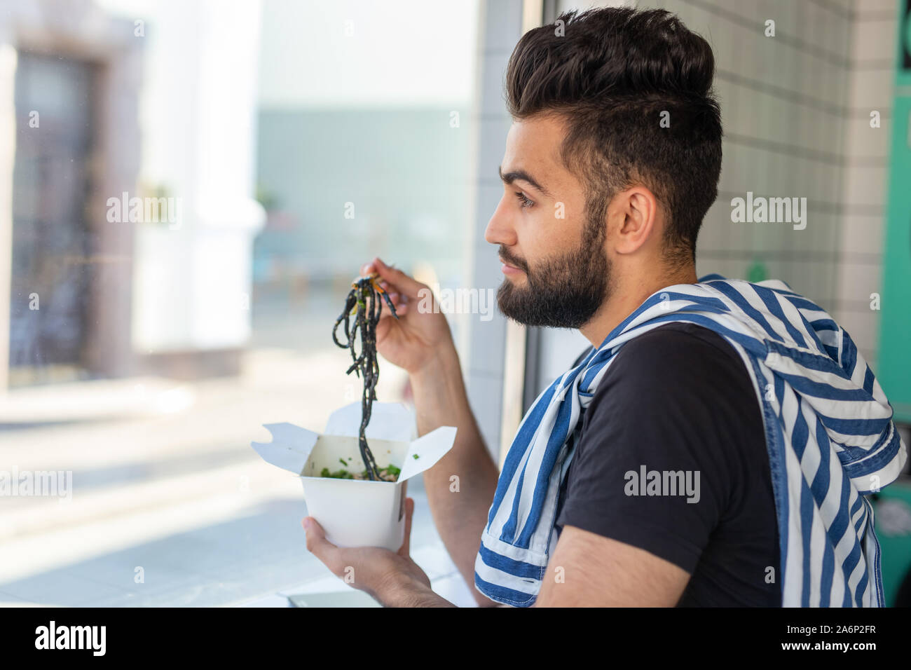 Portrait of a handsome man eating chinese noodles in a cafe and looking ...