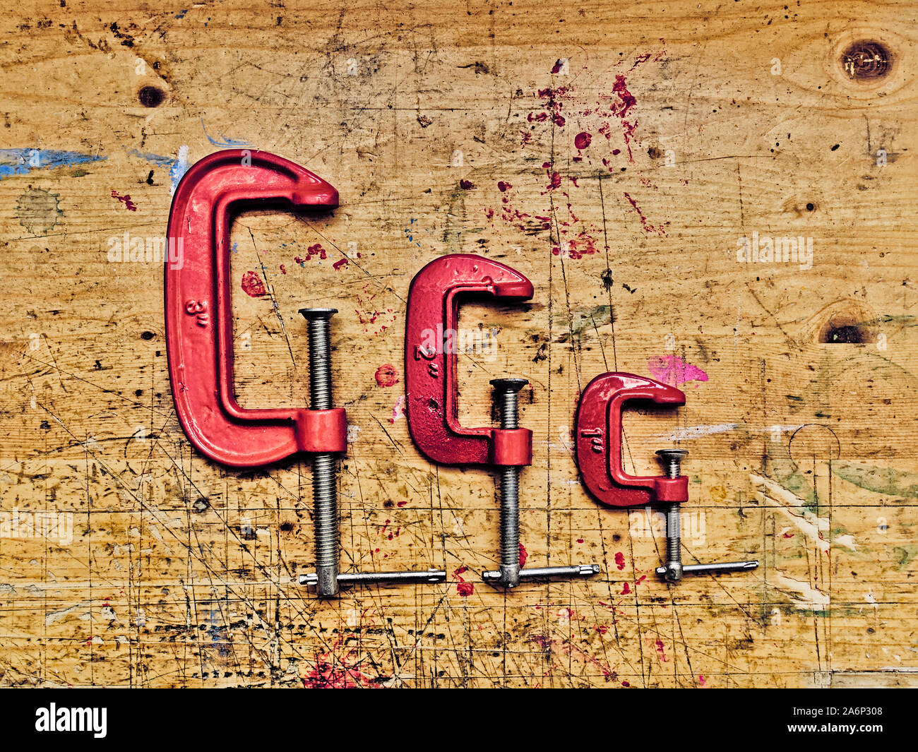 Set of three red metal C clamps on wooden workbench surface background ...