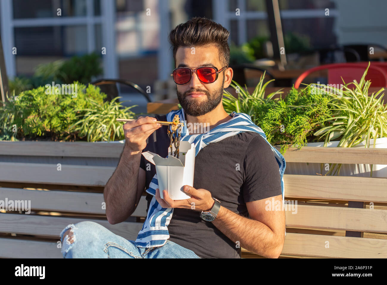 Young male hipster with a mustache and beard is eating chinese noodles ...