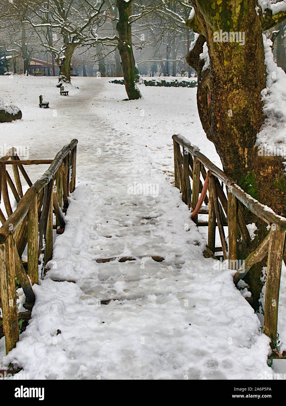 Ice covered wooden bridge path and benches in snow covered Agios ...