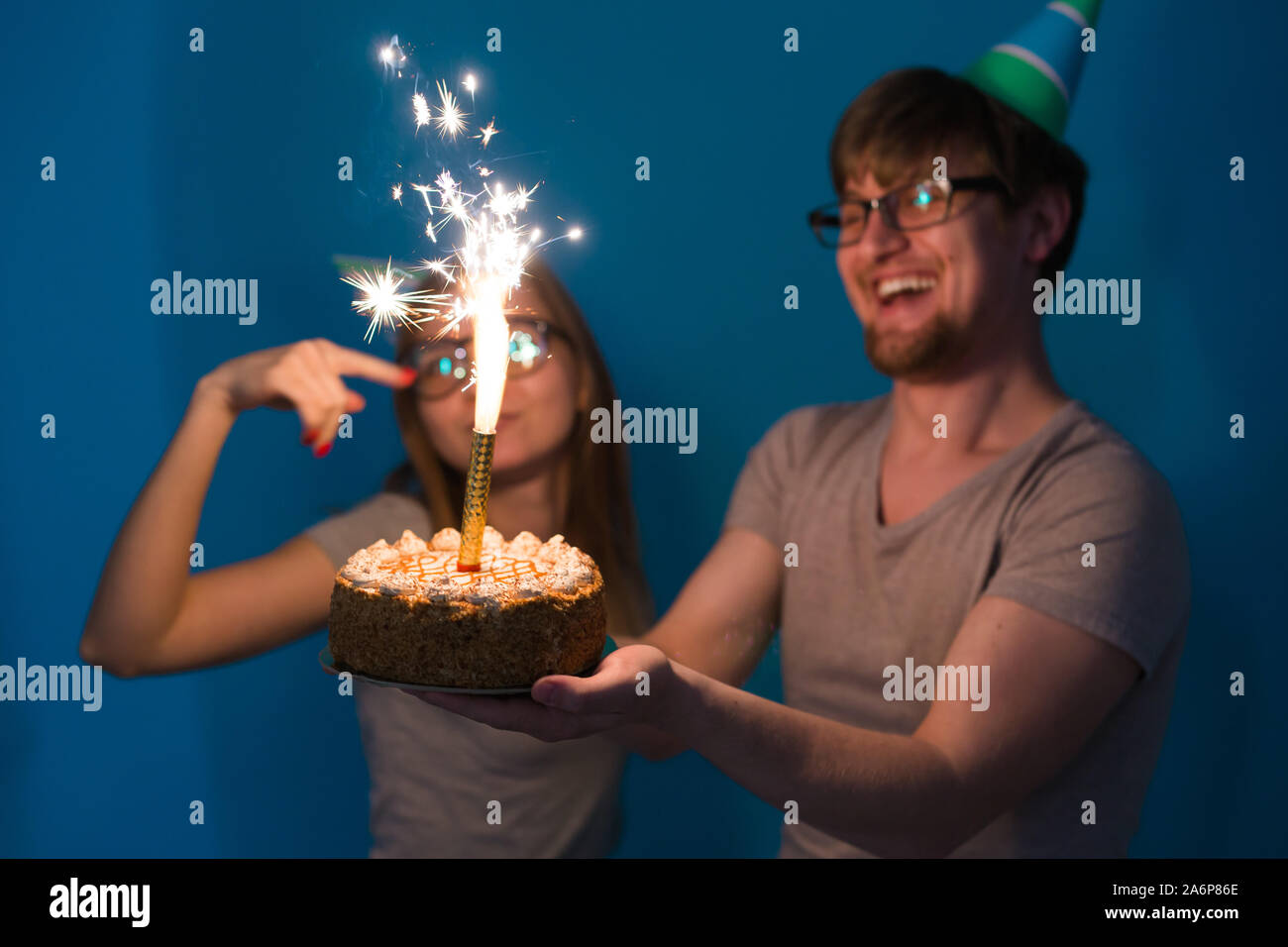Funny young couple in paper caps and with a cake make a foolish face ...