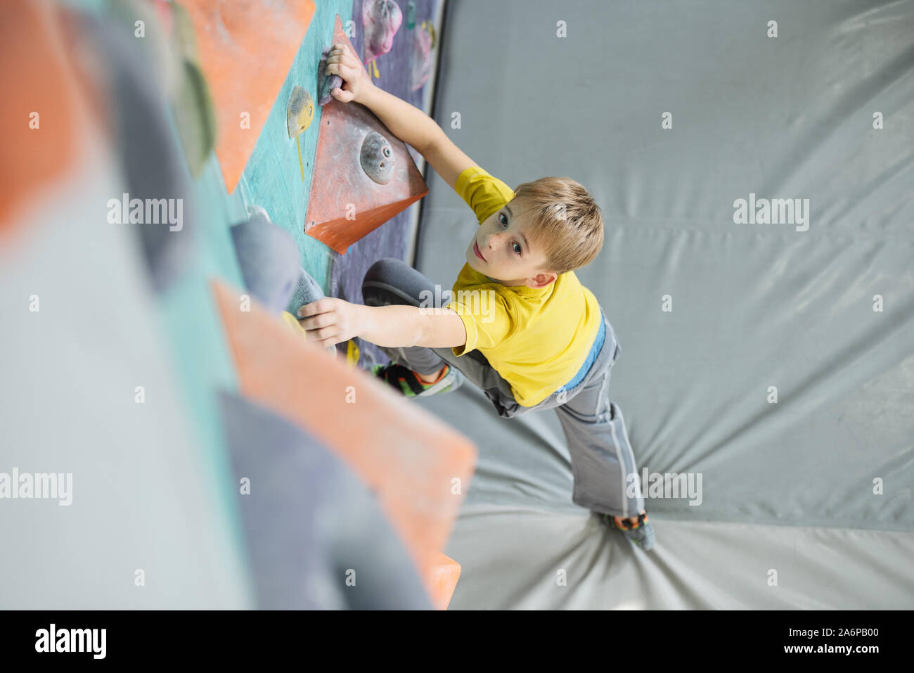 Schoolboy standing on mat and keeping one foot on rock of climbing ...