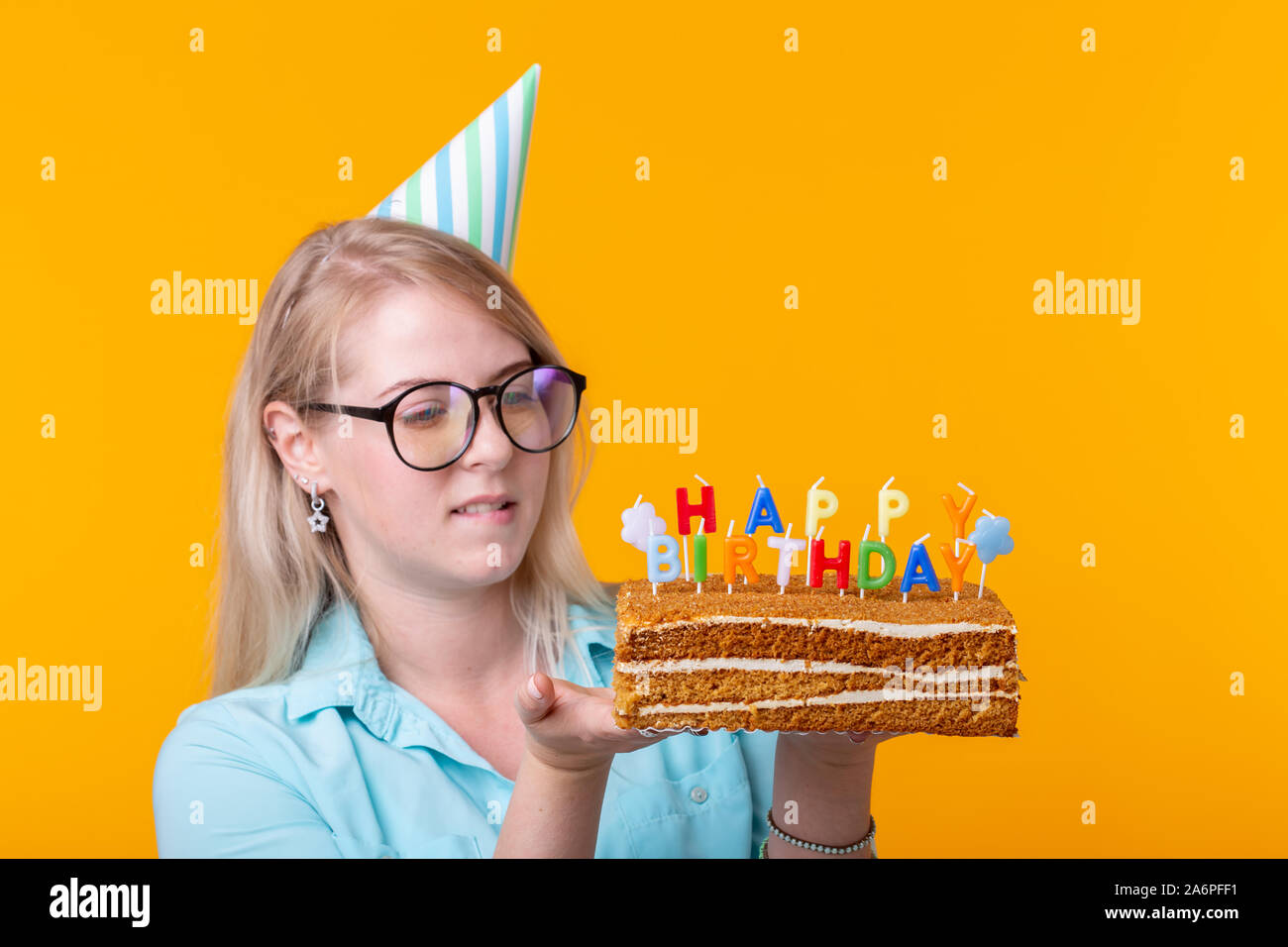 Crazy cheerful young woman in paper congratulatory hat holding cakes ...