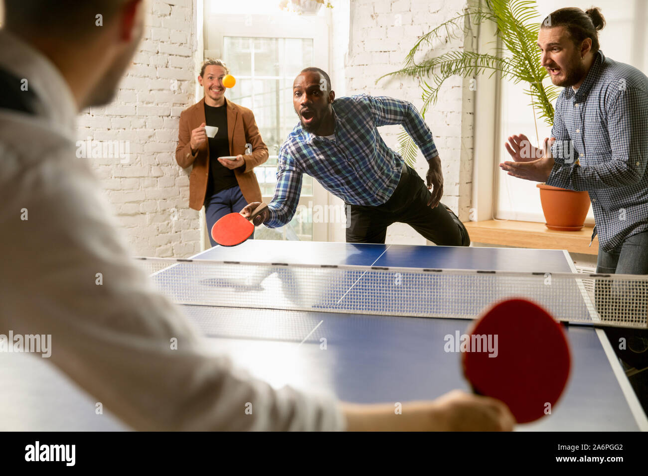 Young people playing table tennis in workplace, having fun. Friends in ...