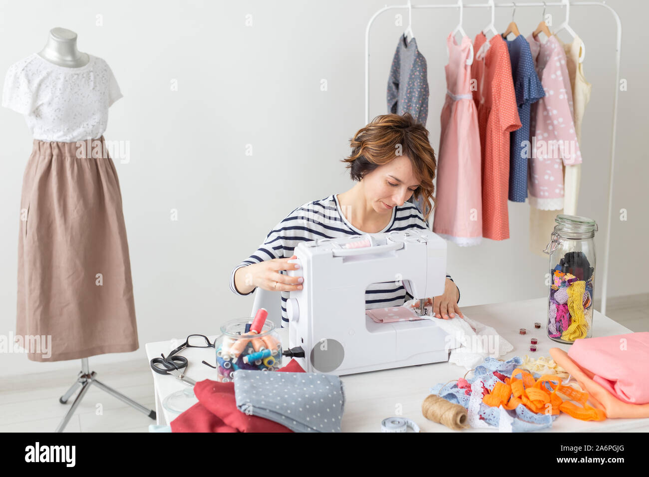 Young seamstress woman sews a new product on a sewing machine sitting ...