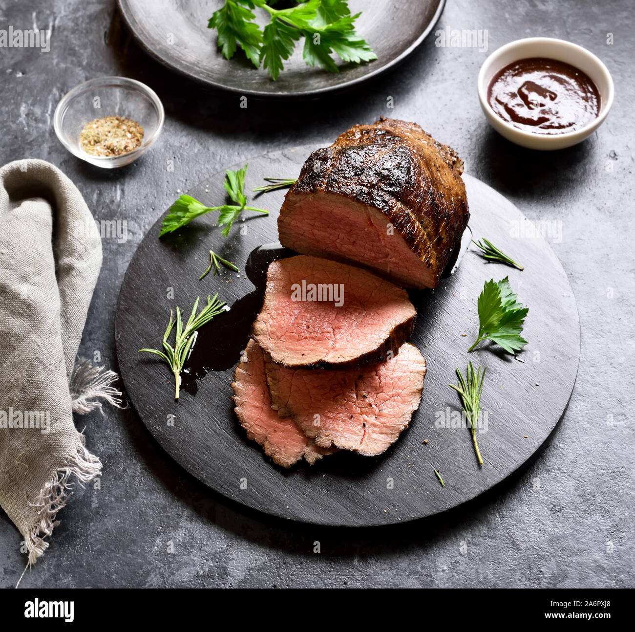 Sliced grilled beef on wooden board over dark stone background. Medium ...