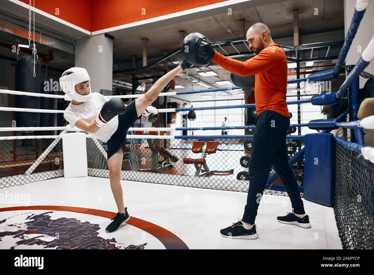 Young kickbox fighter hitting his coach at gym, full length side view ...