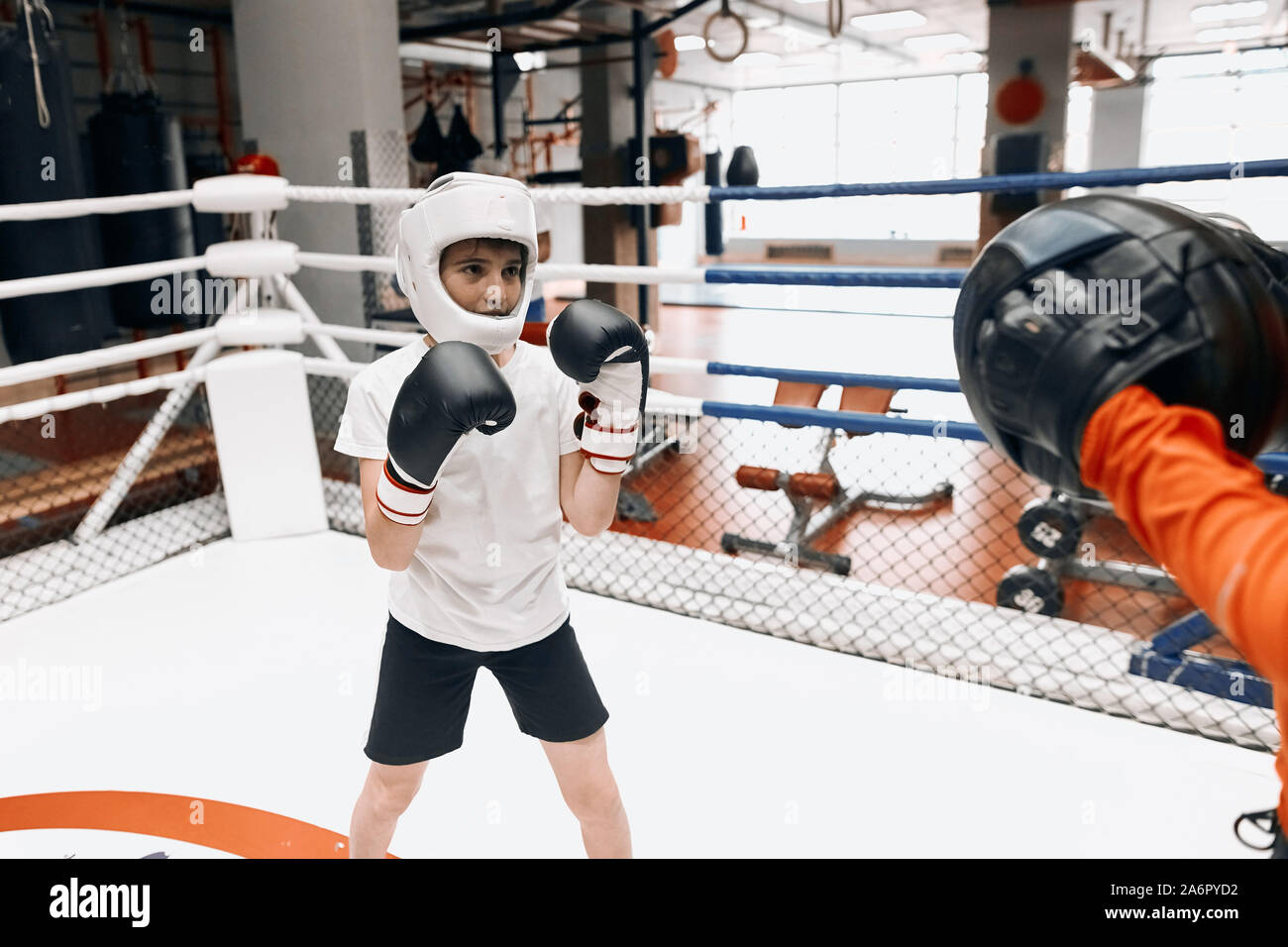 little motivated boy in black boxing gloves going to kick his teacher ...