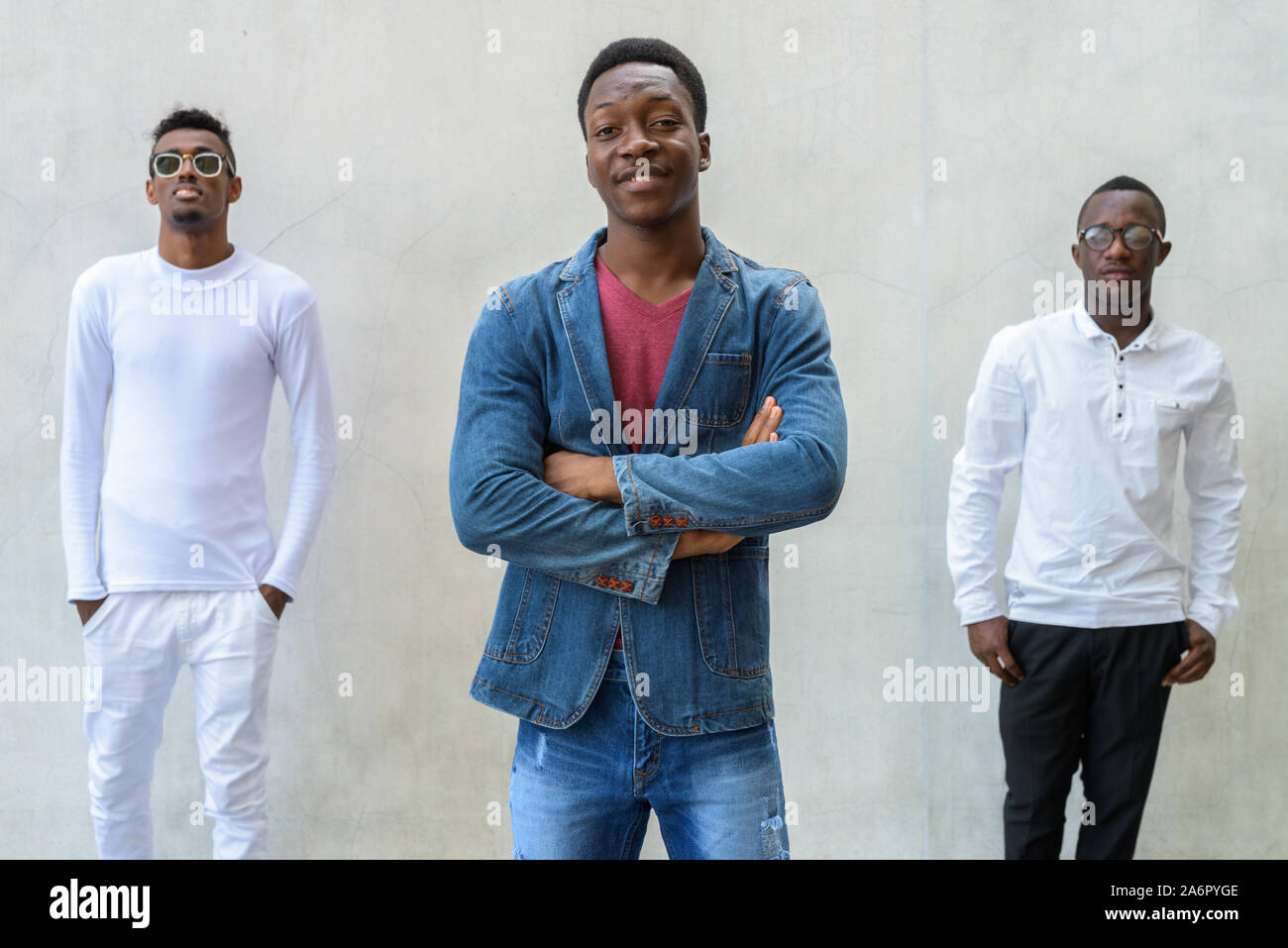 Three young African men hanging out against concrete wall outdoors ...