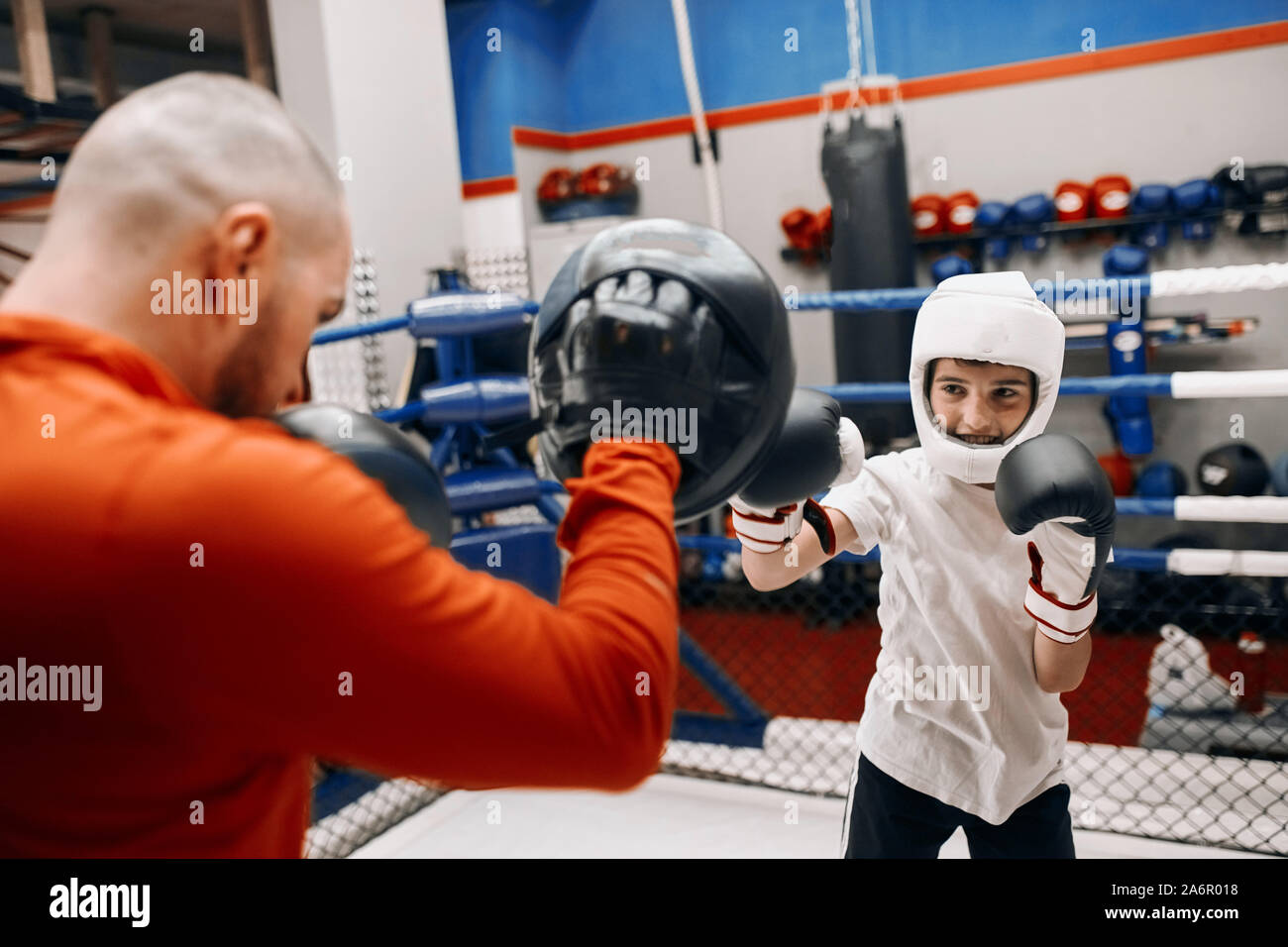 young boy doing kickboxing with muscular sportsman in orange sportswear ...