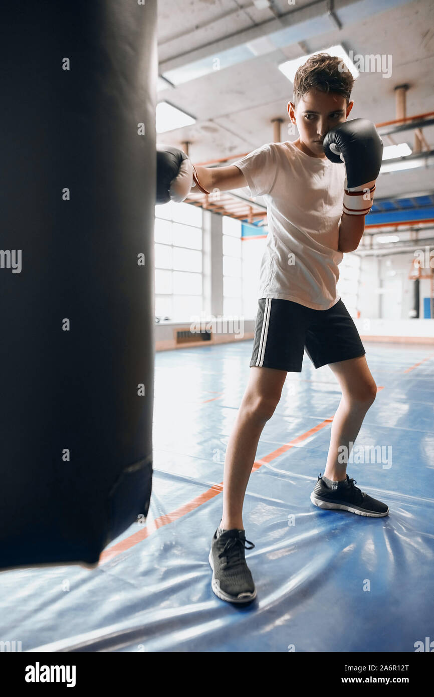 young boxer learns to hit the heavy bag at gym, full length photo ...