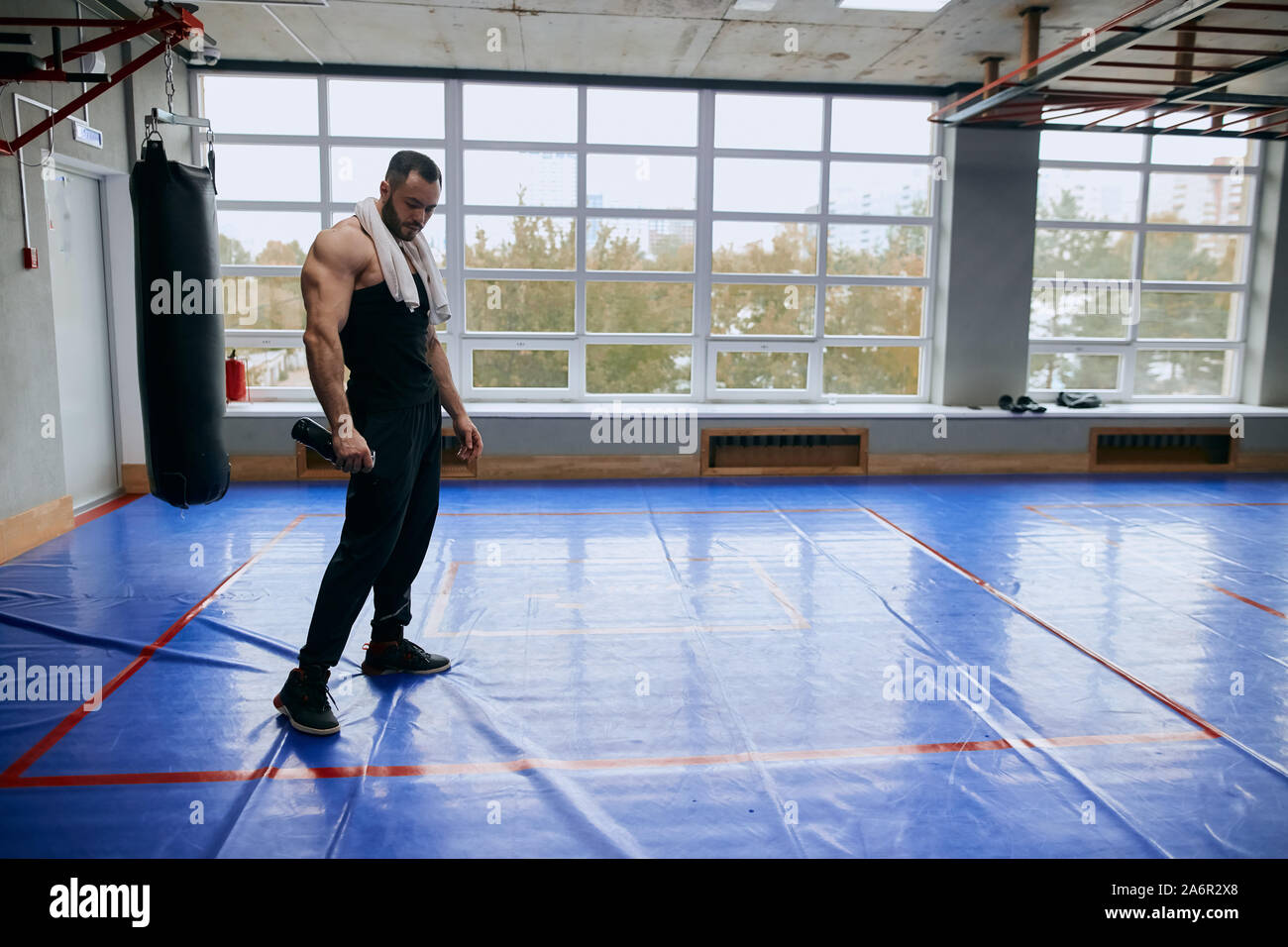tired muscular bodybuilder with water bottle and towel on his shoulder ...