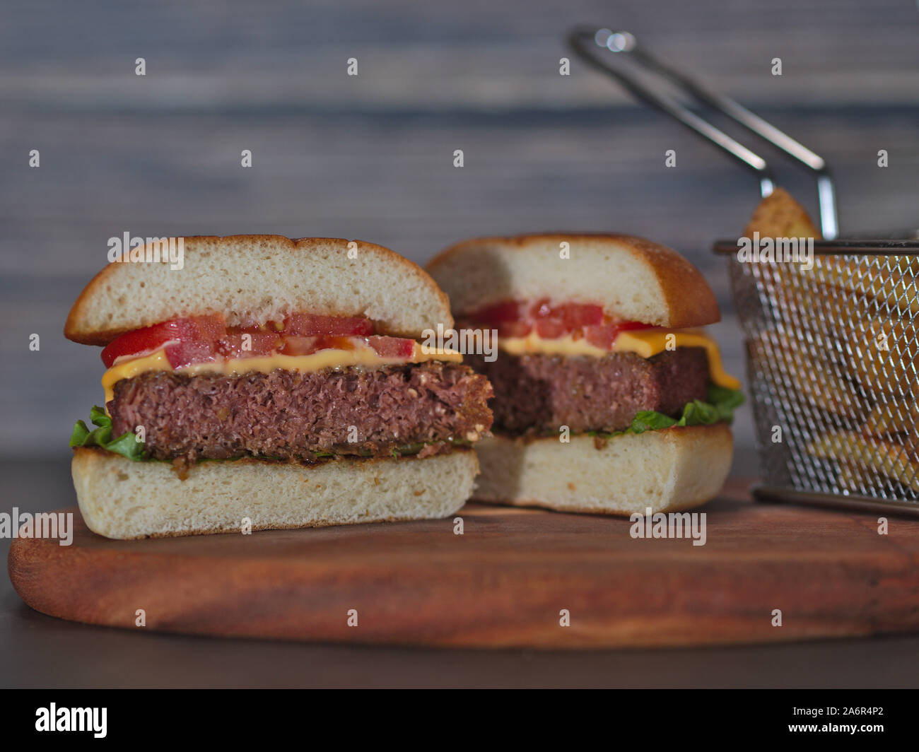 vegan plant based burger cut in half with fries served on wooden tray ...
