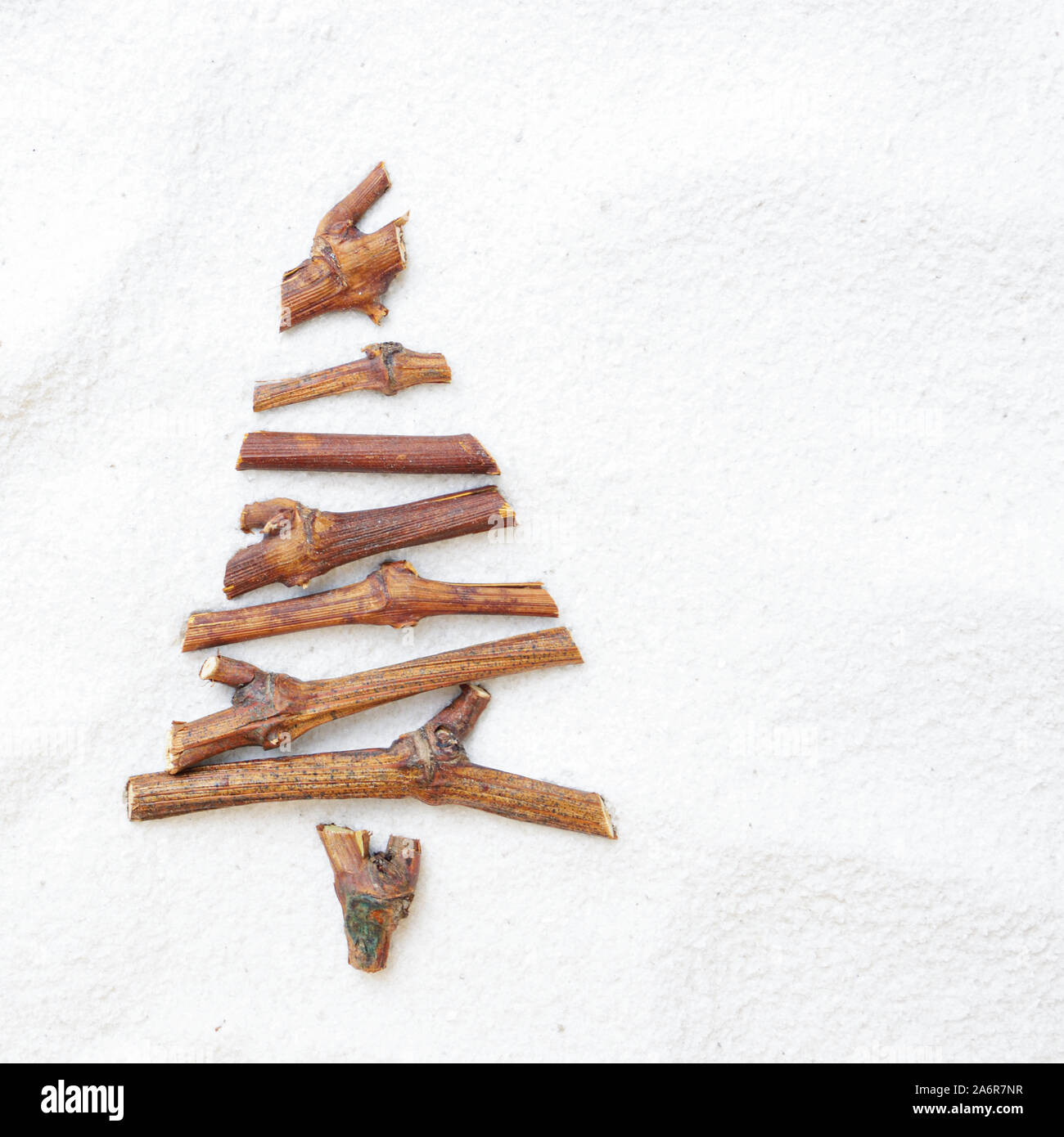Flat lay stylized Christmas tree made of small twigs on snow background ...