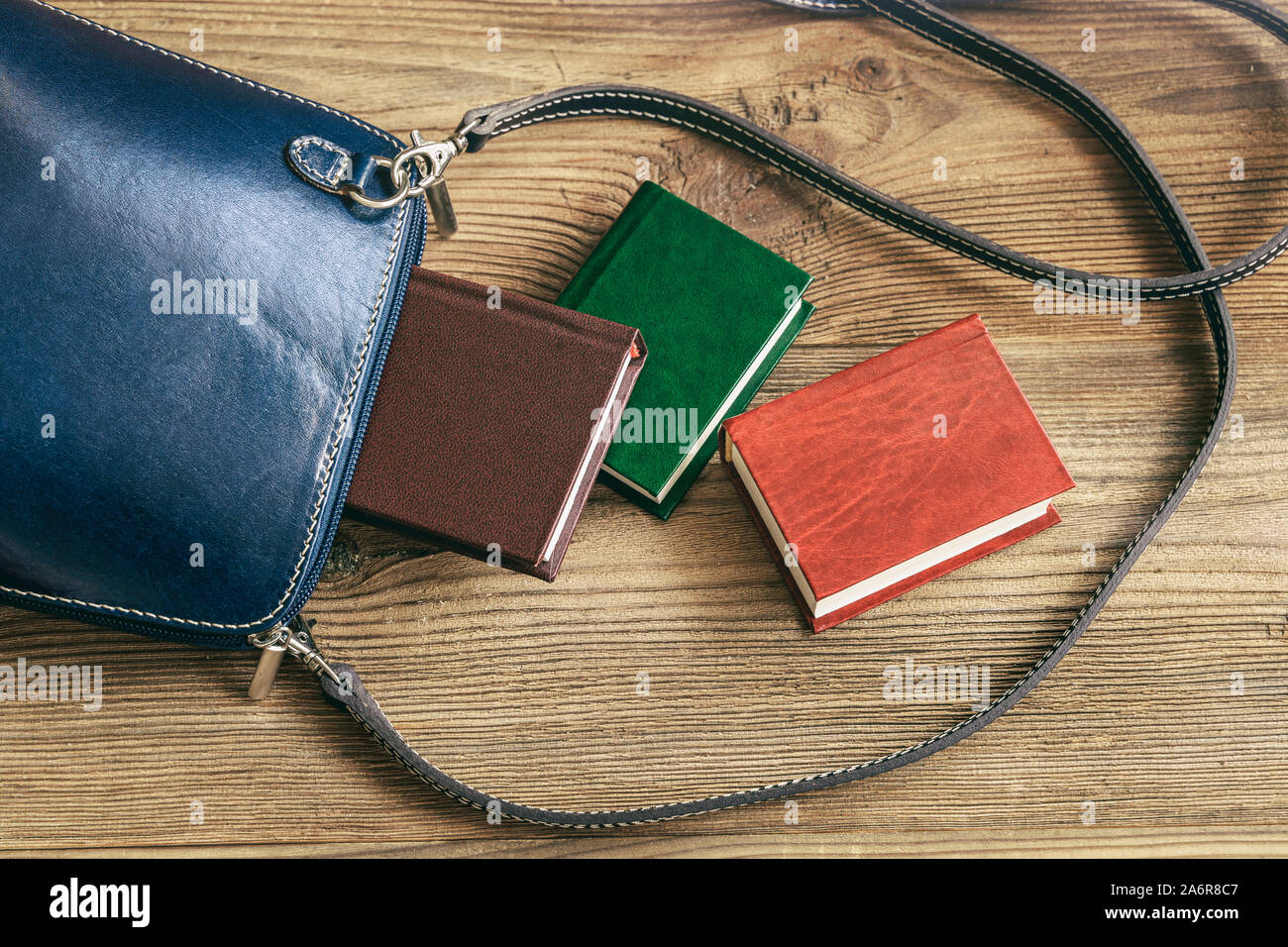 Open blue leather bag on a wooden background with books lying near ...