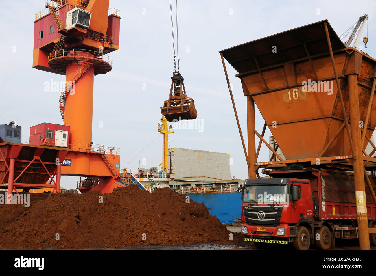 Grab bucket cranes along a quay unload iron ore from a bulk cargo ship ...
