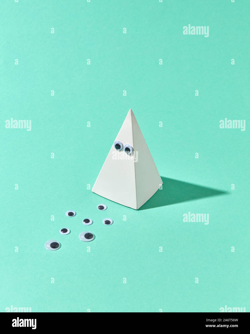 Plaster pyramid with eye pupils on a light turquoise background with ...