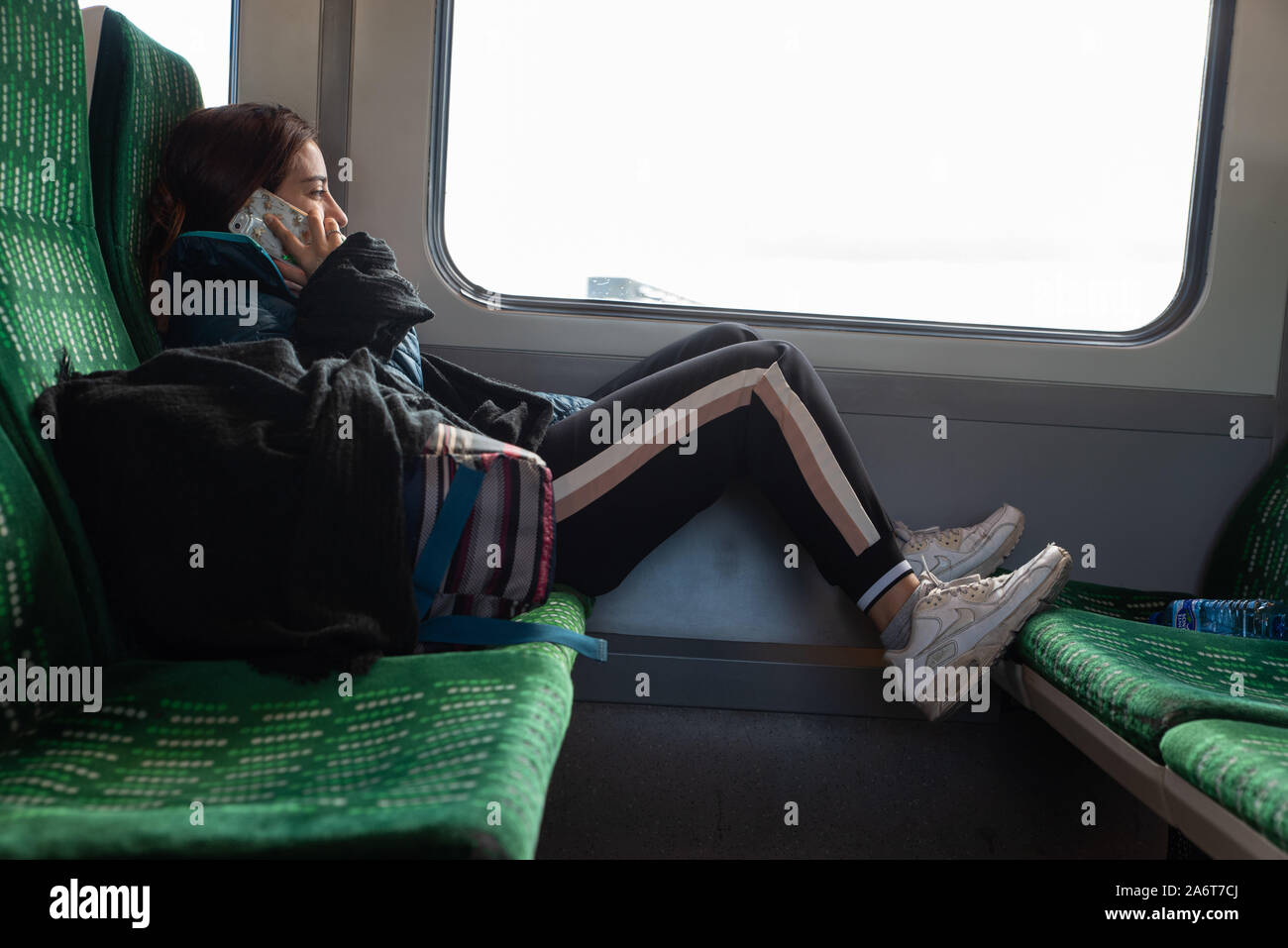 A young woman on the phone with both her feet on a seat in public ...