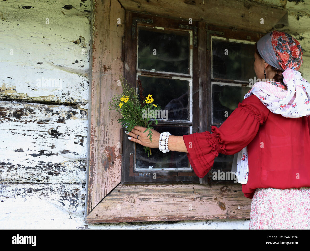 woman in national costume by the window of an old wooden house in ...