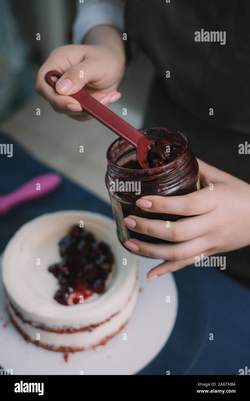 Cook puts jam with berries on the cake with cream. The pastry chef puts ...