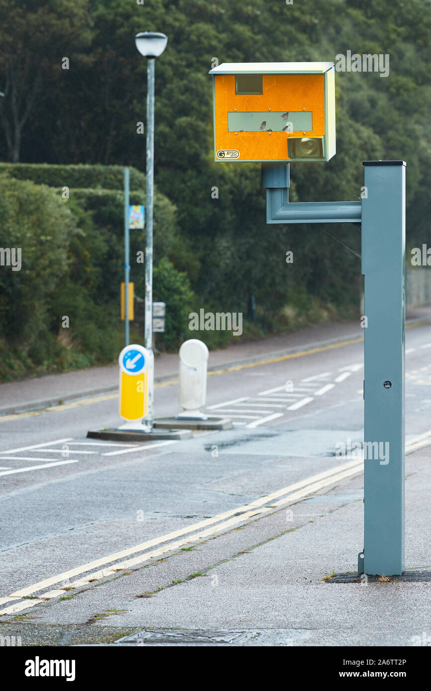 Gatso speed camera, in distinctive yellow, on a pavement next to a road ...