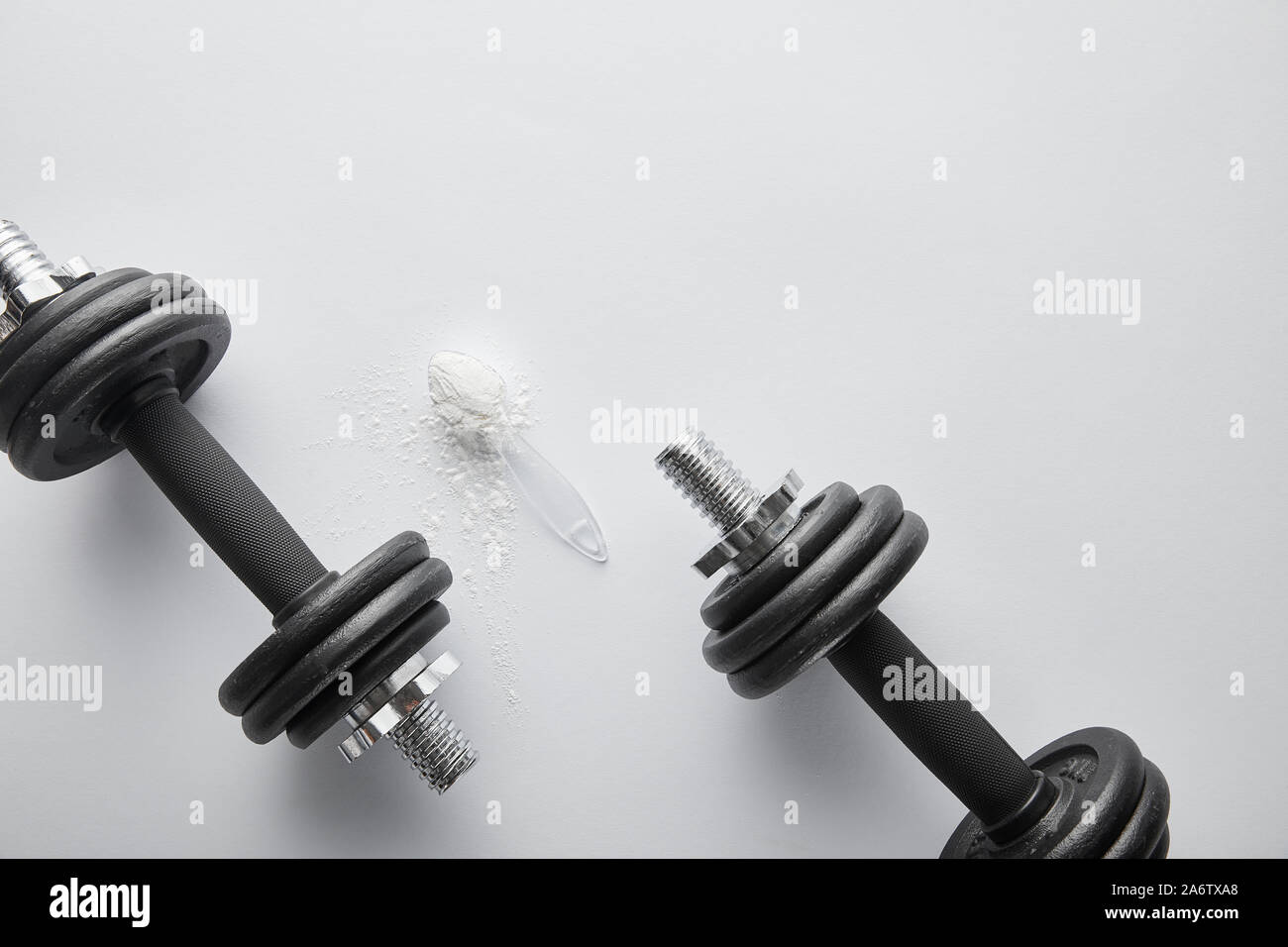 top view of spoon with protein powder near heavy dumbbells on white ...