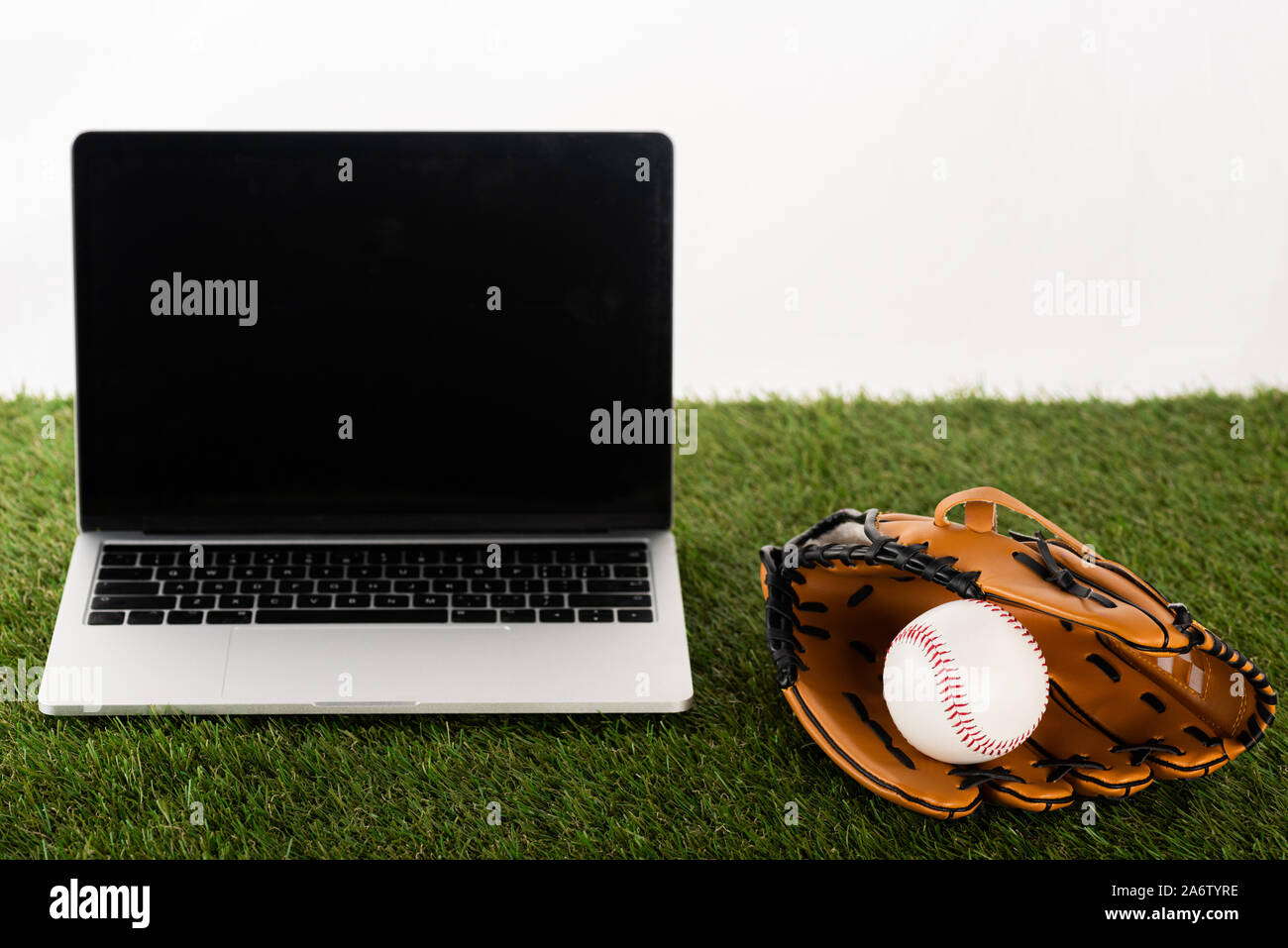 baseball glove and ball near laptop with blank screen on green grass ...