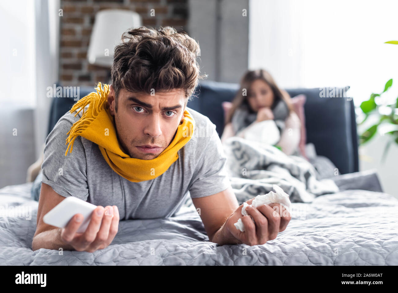 selective focus of sad and sick boyfriend holding napkin and smartphone ...