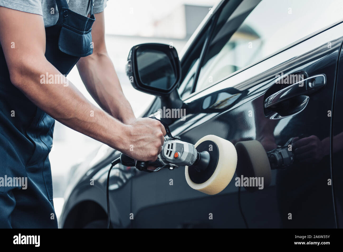 partial view of car cleaner polishing car door with buffer machine ...