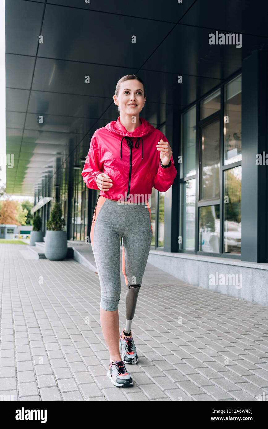 full length view of smiling disabled sportswoman running on street ...