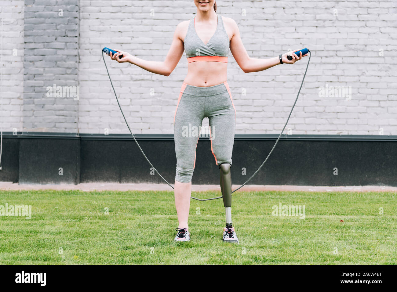 partial view of smiling disabled sportswoman with jump rope on grass ...