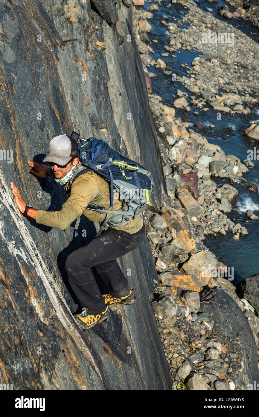 Hiker scrambling up vertical rock wall. Free solo up rock climb in ...